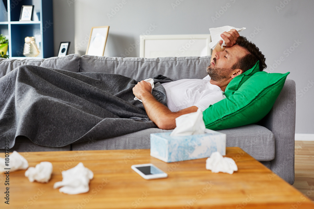 Sick man with fever lying on couch at home Stock Photo | Adobe Stock