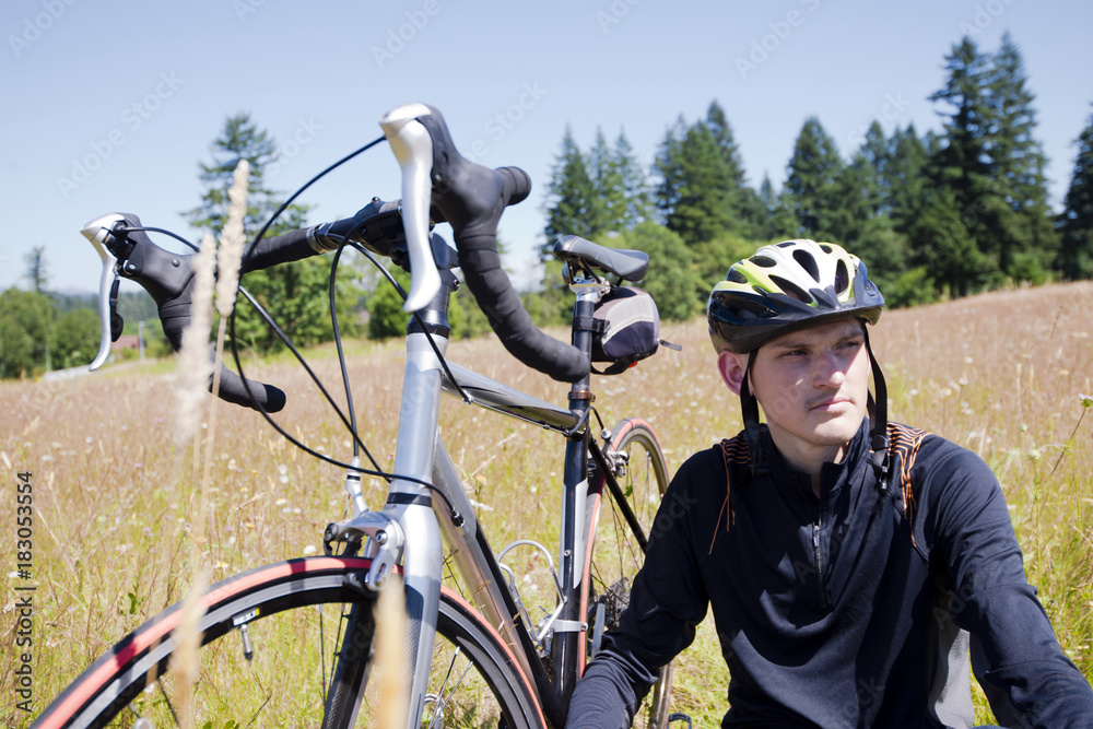 Cyclist resting after bicycle ride sitting in tall yellowed grass in an ...