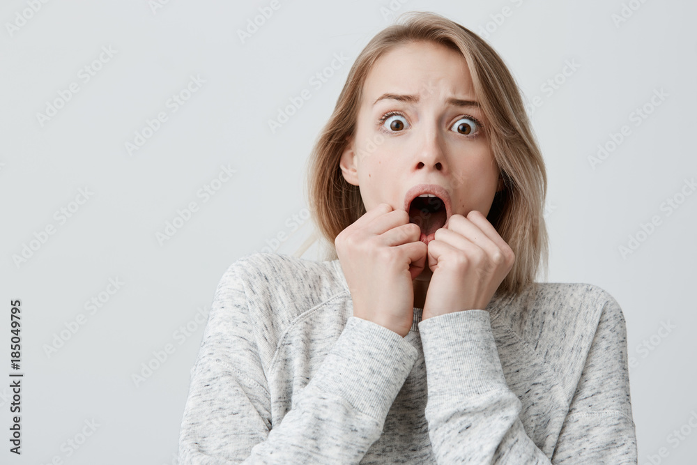 Astonished terrified attractive young blonde with dyed hair female in sweater having scared face ...