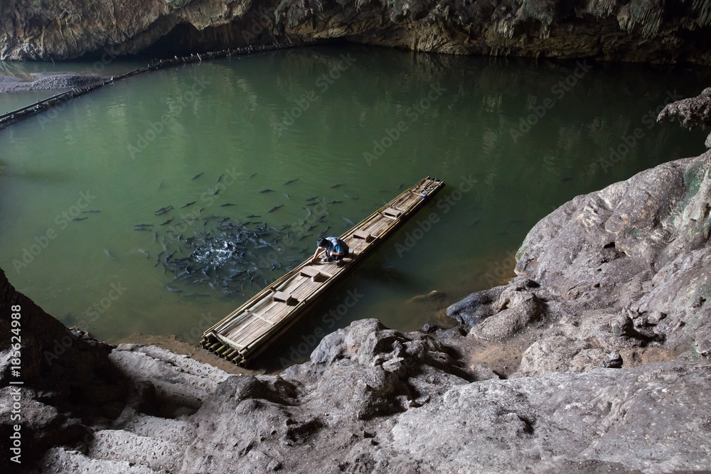 Man feeds fish / Man on a bamboo boat feeding fish in a cave/ fish that ...