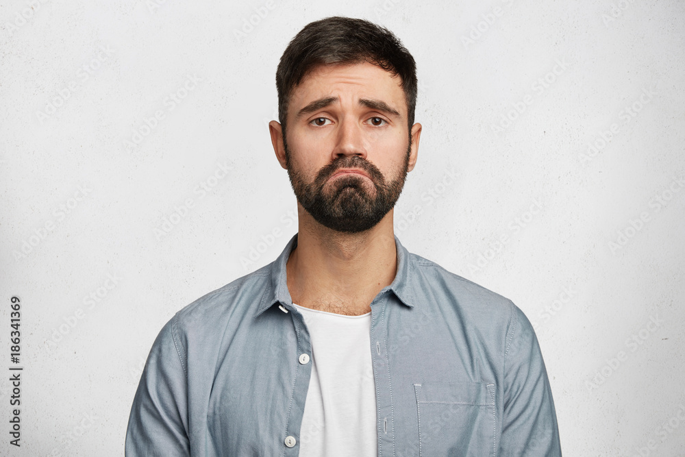 Horizontal shot of attractive male model with unhappy expression curves ...