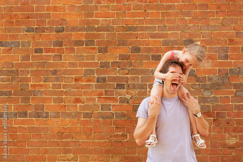 Girl getting shoulder carry from father with covering his eyes by brick ...