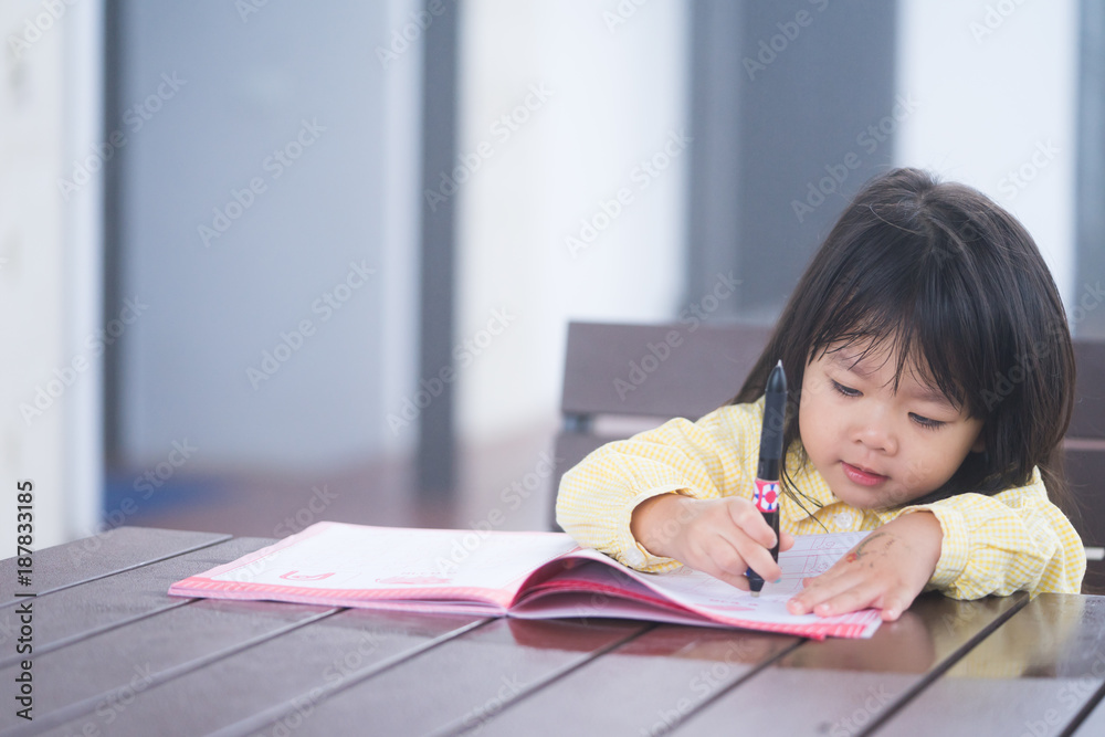 Cute little girl doing homework, reading a book, coloring pages ...