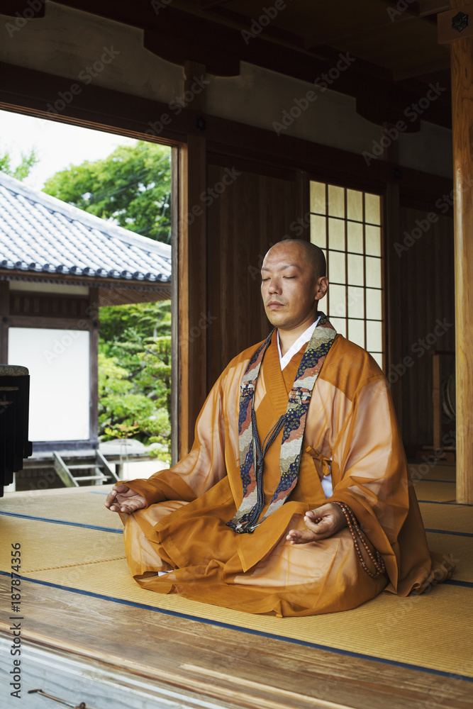 Buddhist monk with shaved head wearing golden robe sitting cross legged ...