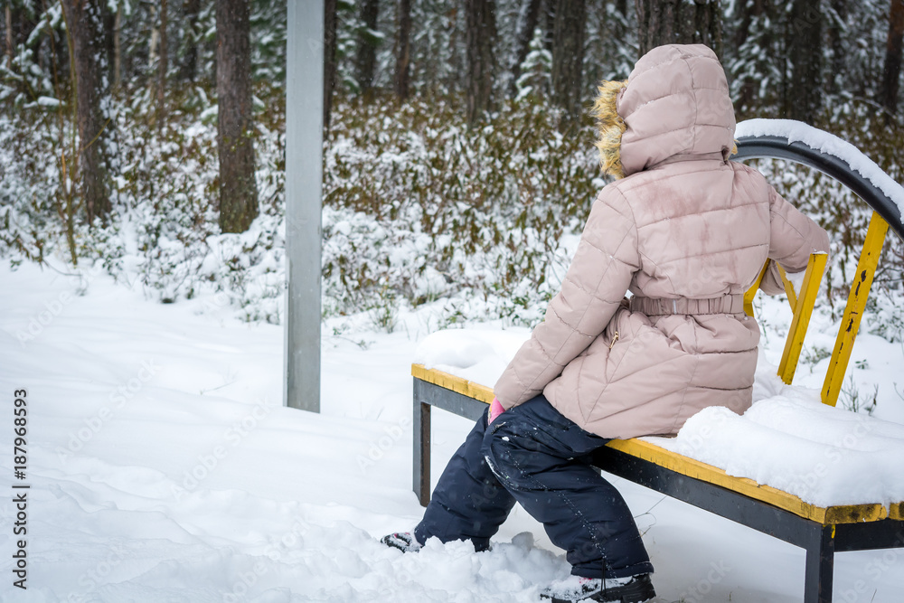 Sad girl in a parka sitting on a snowy bench in winter Park Stock Photo ...