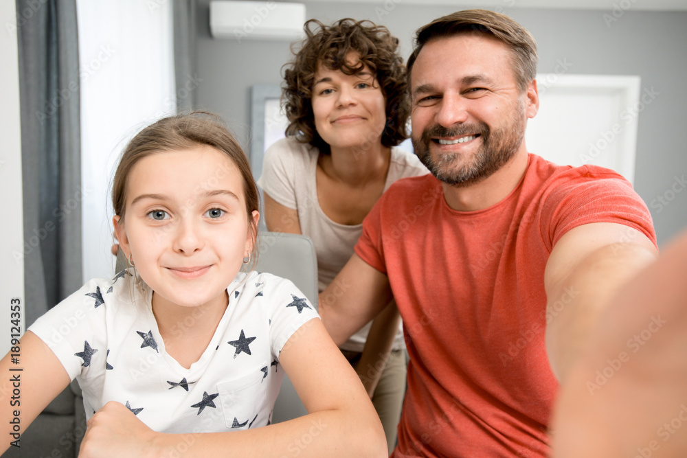 Loving family of three with wide smiles taking selfie together while ...