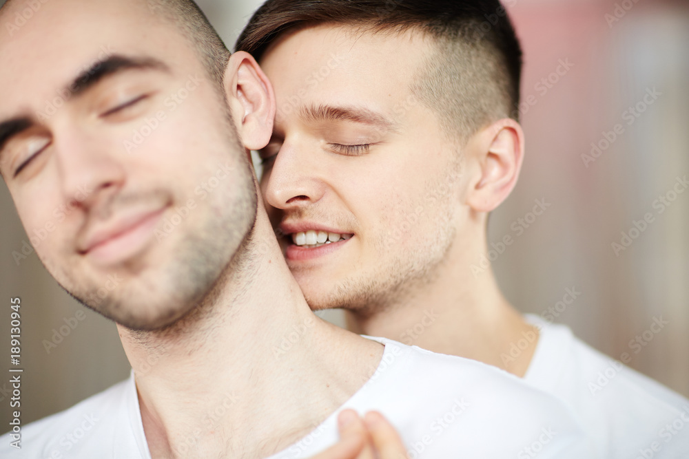 Amorous young gay man touching neck of his sweetheart and both smiling ...