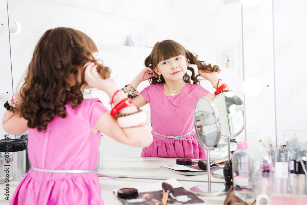beautiful little girl in the mirror preening and using makeup to ...