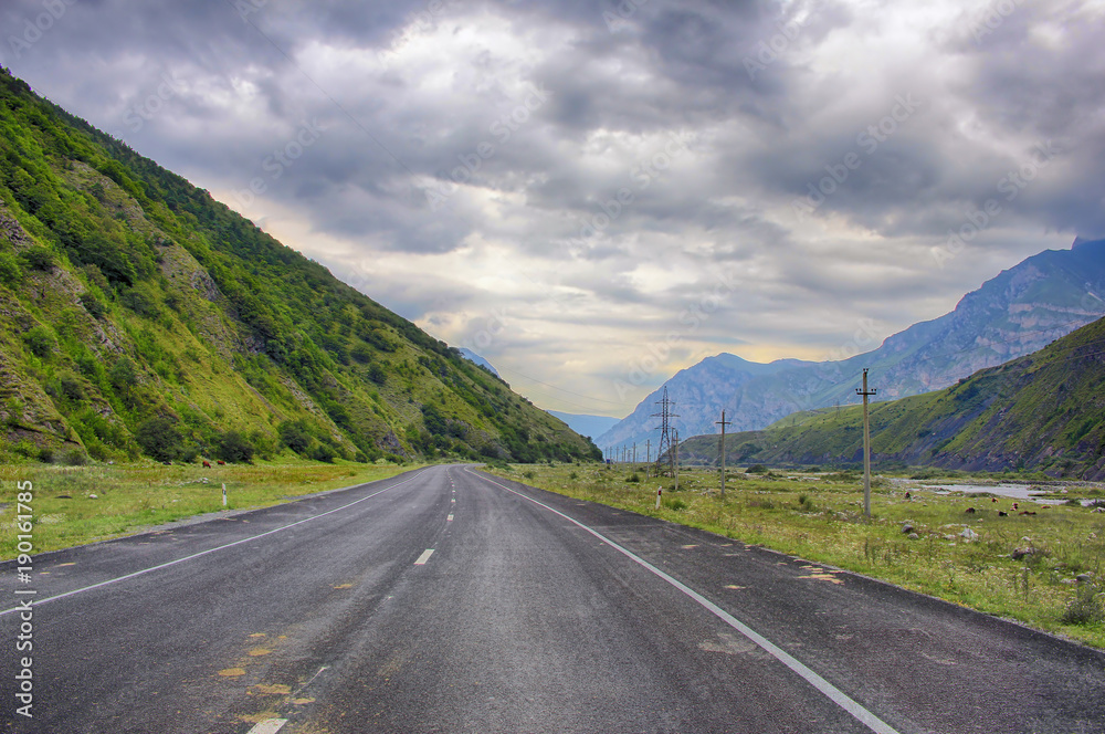 Highway running away through the mountain valley between high green ...