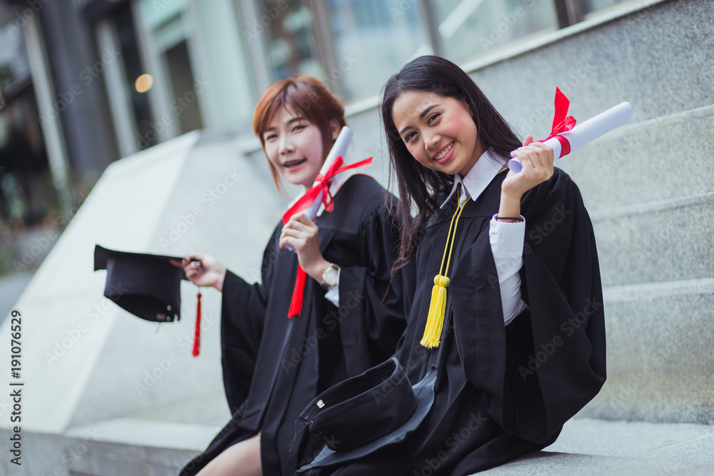 Portrait of Two happy graduated young girls in graduation gowns holding ...