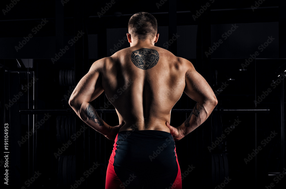 Huge weightlifter stands with his back to the camera and shows his huge ...