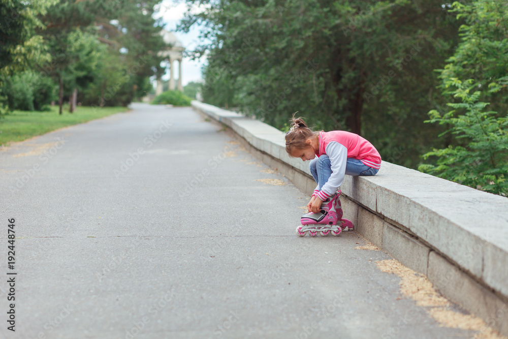 Little girl sitting on parapet and putting on rollers in the park Stock ...