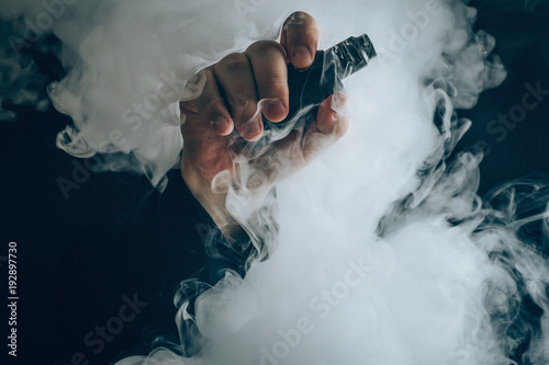 Man hand shows vape device at cloud of vapor background. Vape concept ...