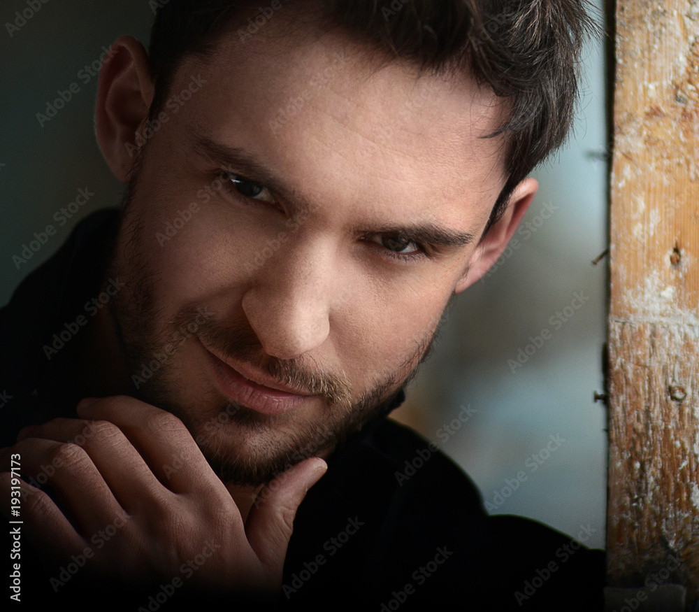 Mysterious handsome man with sneaky look. man with beard smiling. sexy guy in a dark jacket with ...