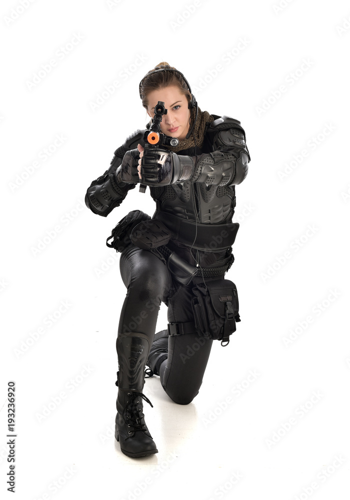 full length portrait of female wearing black tactical armour, crouching ...