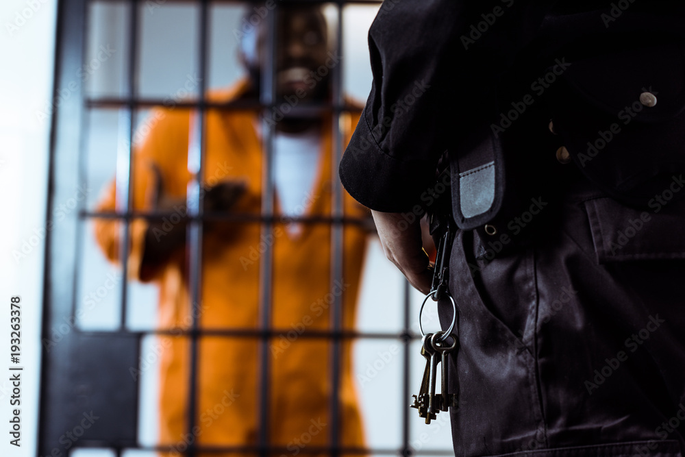 cropped image of security guard standing near prison bars with keys ...