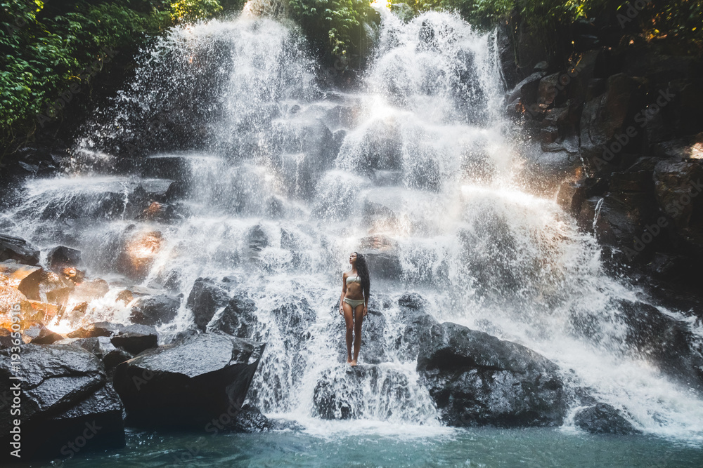 Woman enjoying under stream of big and beautiful cascade waterfall ...