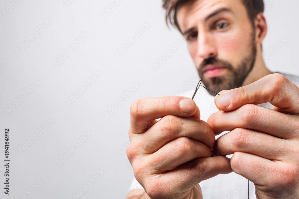 Serious and concentrated guy is trying to put a thread through an eye ...