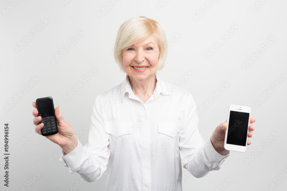 Happy senior woman is holding an old phone with buttons and a new phone ...