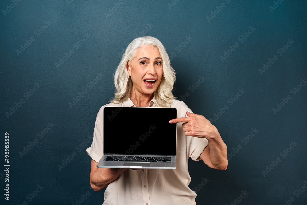 Cute mature old woman showing display of laptop computer pointing ...