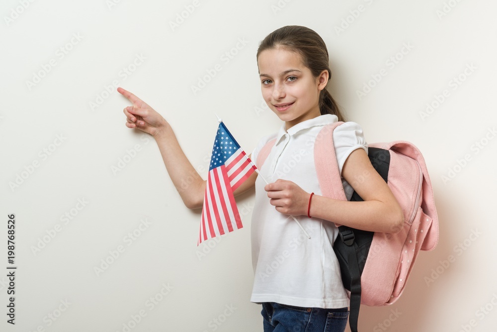 School child with a backpack holds the US flag, background bright wall ...