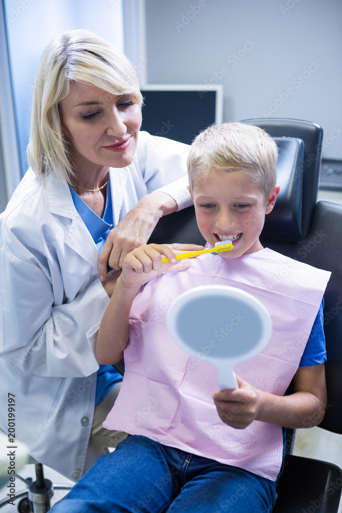 Dentist assisting young patient while brush teeth Stock Photo | Adobe Stock