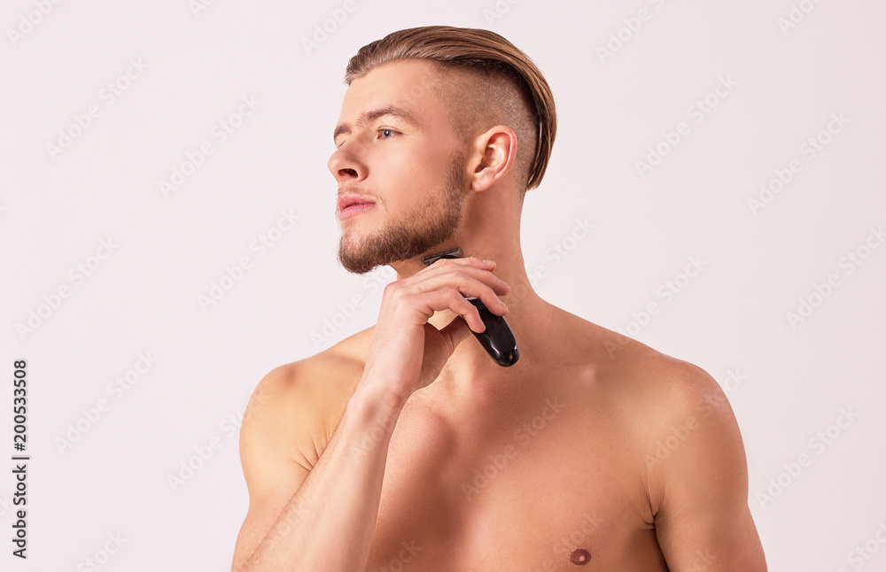 Shirtless handsome man shaving his beard with electrical shaving ...