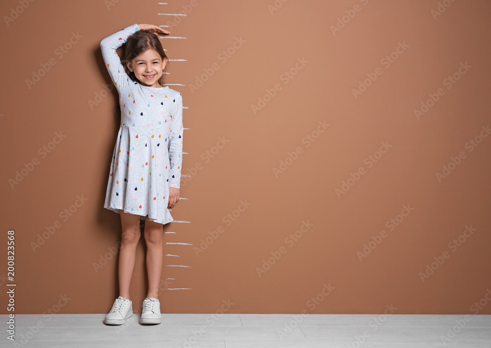Little girl measuring her height near color wall Stock Photo | Adobe Stock