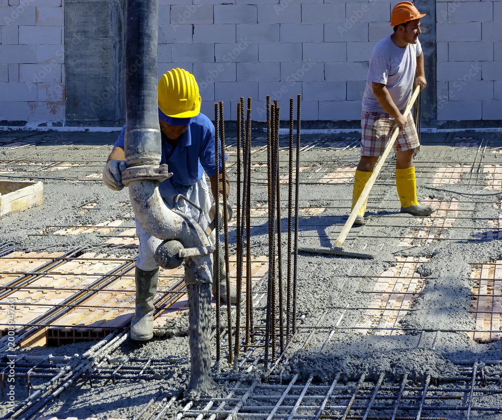 Construction worker compacting liquid cement in reinforcement form work ...