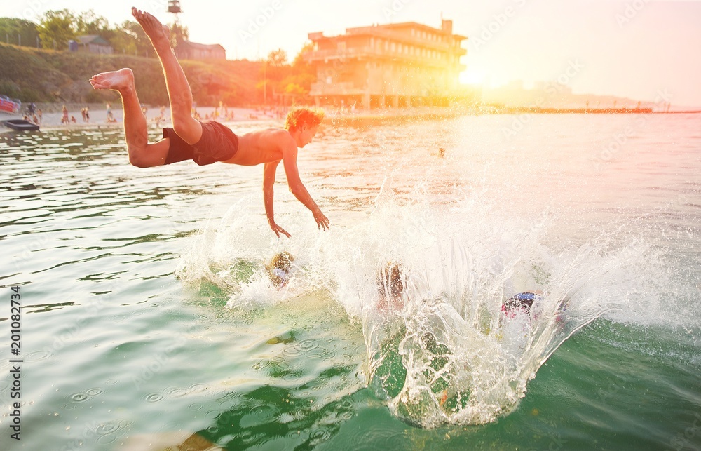 Group of happy people having fun jumping in the sea water from a pier ...