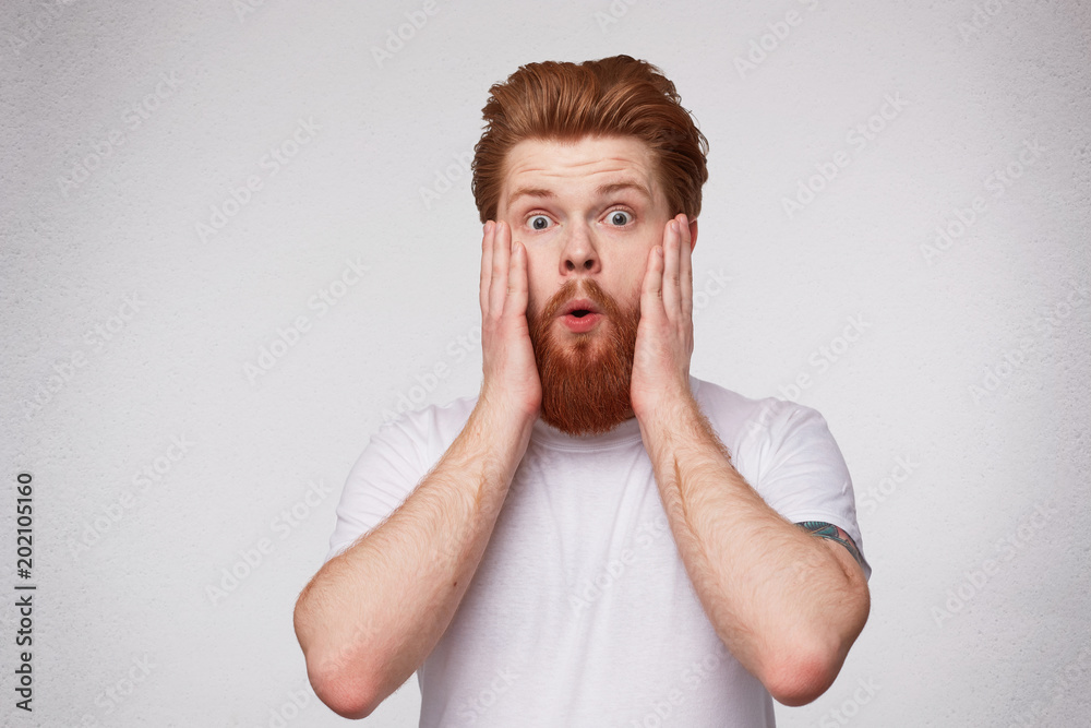 Indoor shot of shoked stupefied young ginger male looks with frightened ...