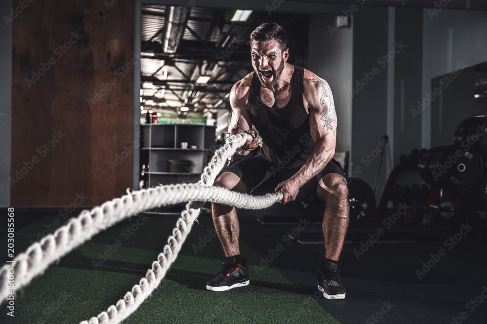 Muscular powerful aggressive man working out with rope in functional ...