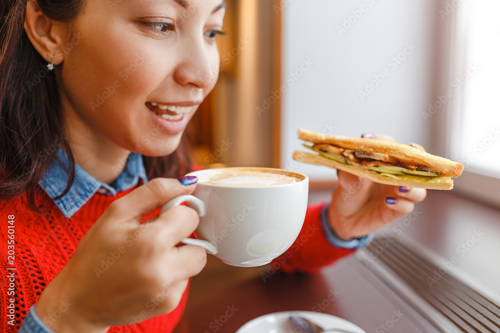 young girl student eating a sandwich and drinking coffee in a cafe near ...