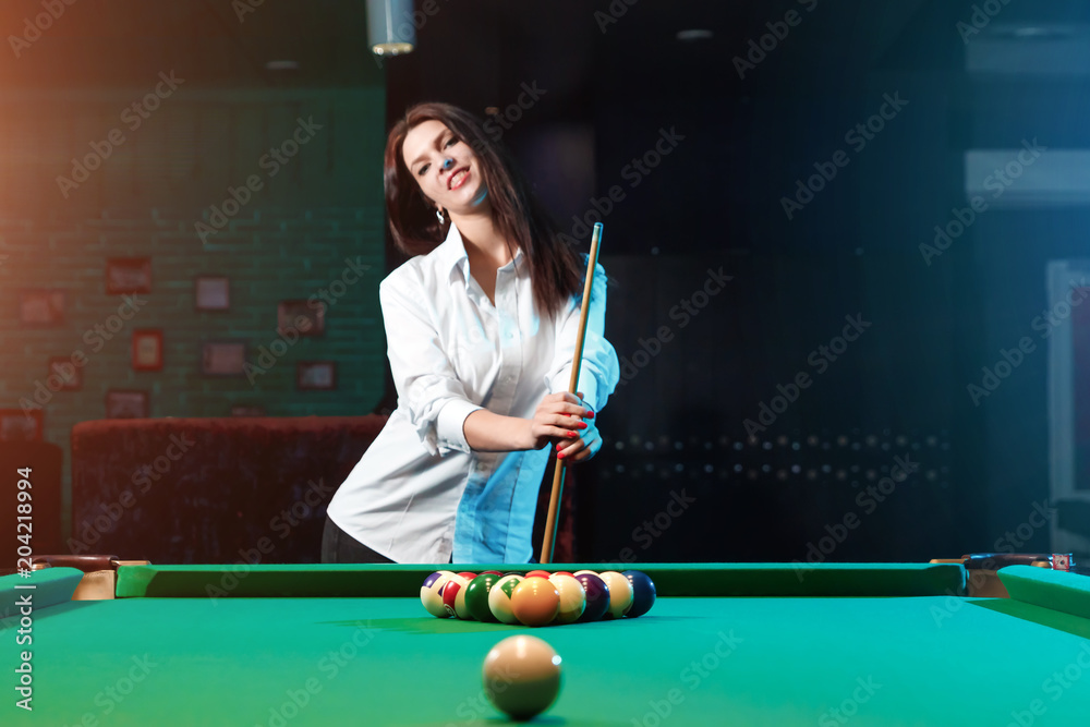 Young beautiful girl posing at a billiard table. Dark background ...