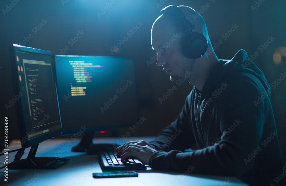 cybercrime, hacking and technology concept - male hacker with headphones and coding on laptop ...