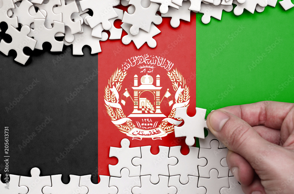 Afghanistan flag is depicted on a table on which the human hand folds a ...