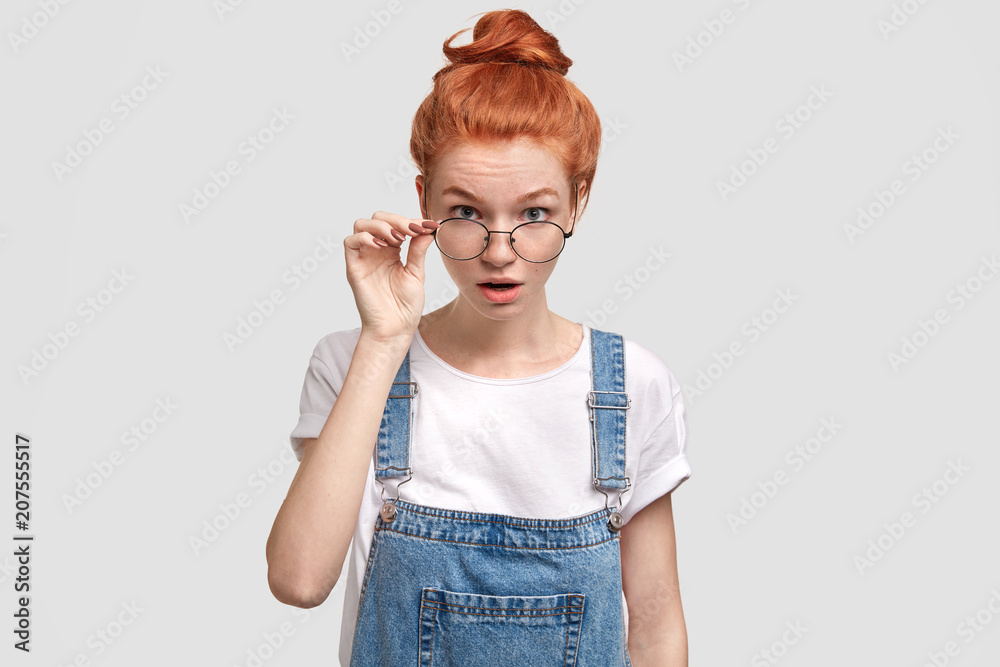 Photo of surprised ginger woman looks scrupulously at camera, reads ...