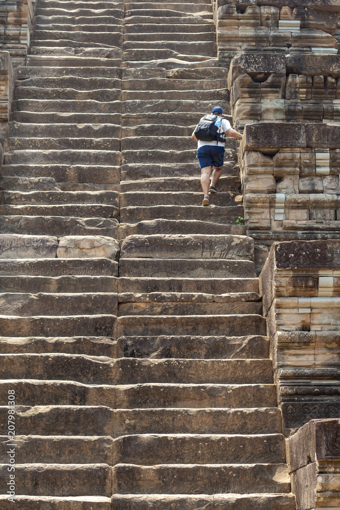 Man tourist climbs the high stair of ancient temple. Endless steps of ...