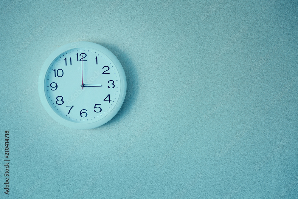 Round white clock on a blue wall. The clock shows three o'clock in the ...