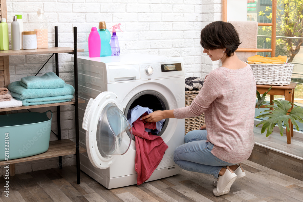 Young woman putting clothes into washing machine at home Stock Photo ...