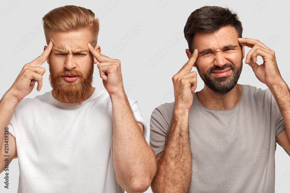 Stressed two unshaven young male friends keep fore fingers on temples ...