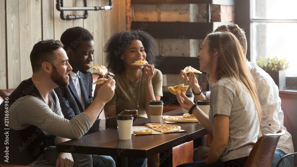 Smiling multiracial friends eating pizza and drinking coffee, laughing ...