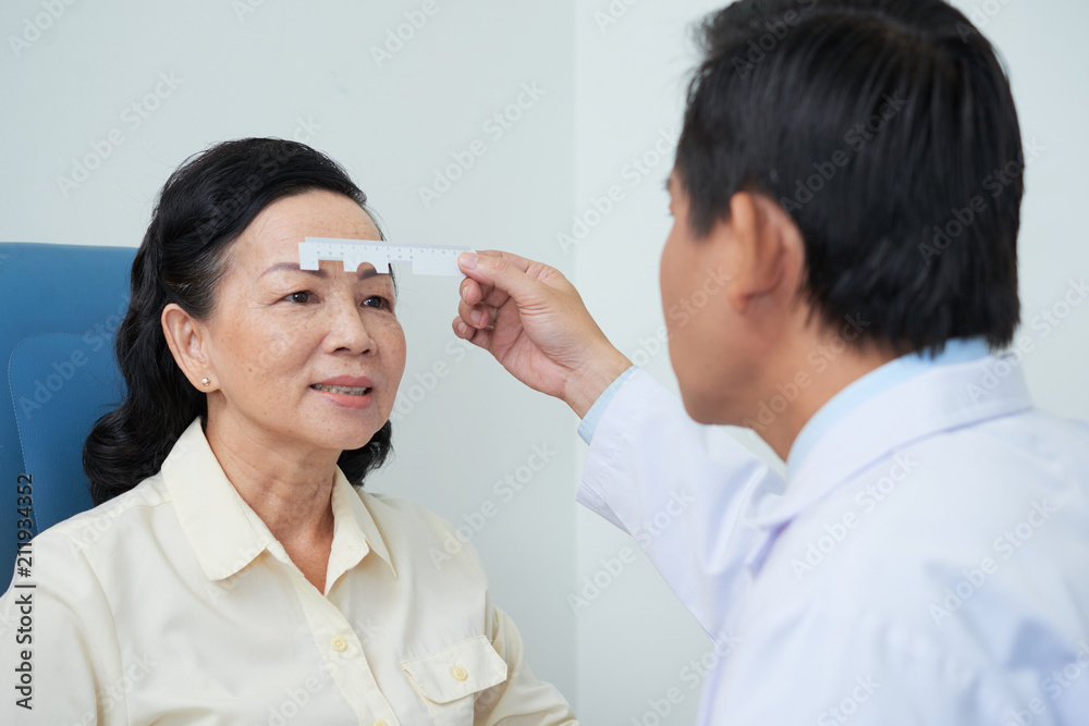 Professional oculist using special ruler and measuring eyes of mature ...