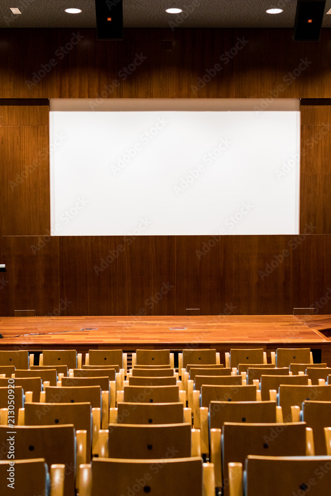 Conference room with wooden seating, stage and large cinema screen in ...