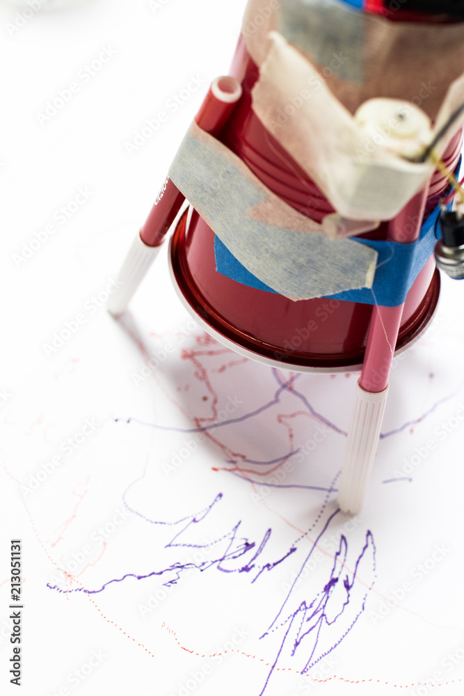 Plastic cup with DC motor and batteries writing with a marker on white ...