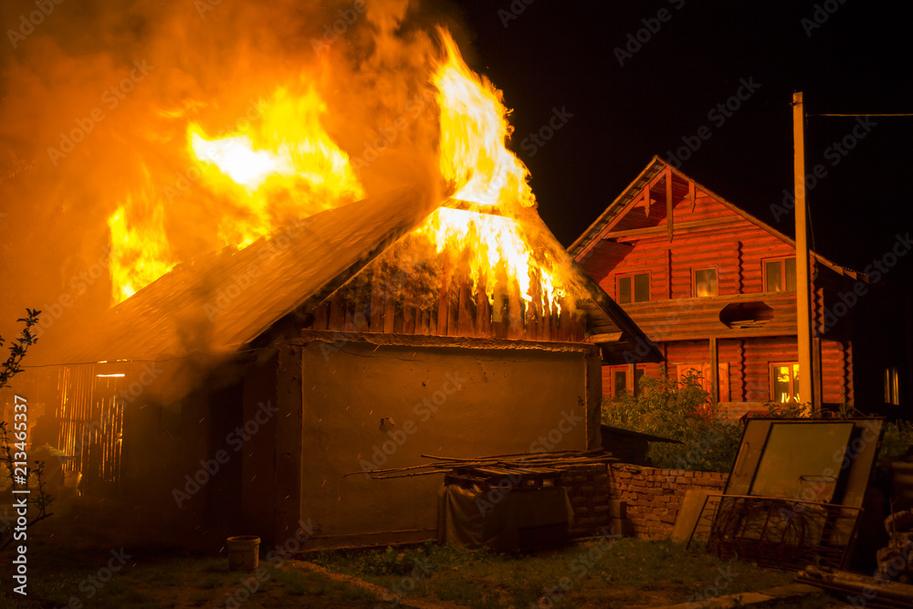 Wooden barn burning at night. High orange fire flames, dense smoke from ...