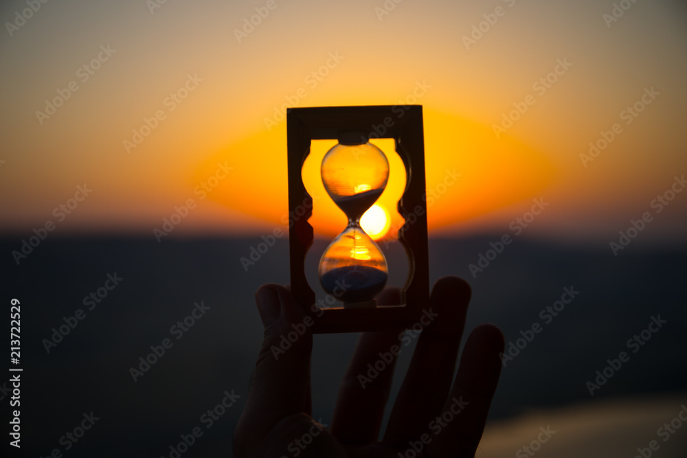 Life time passing concept. Hand holding hourglass with sunset sky ...