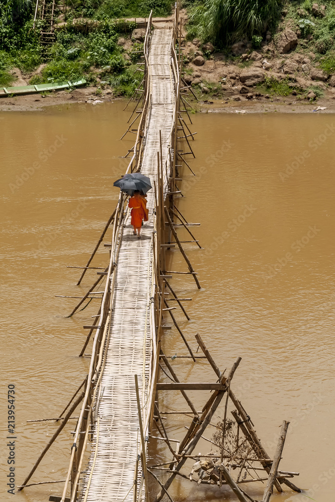 Buddhist monks cross the Nam Khan river on a bamboo bridge, protecting ...