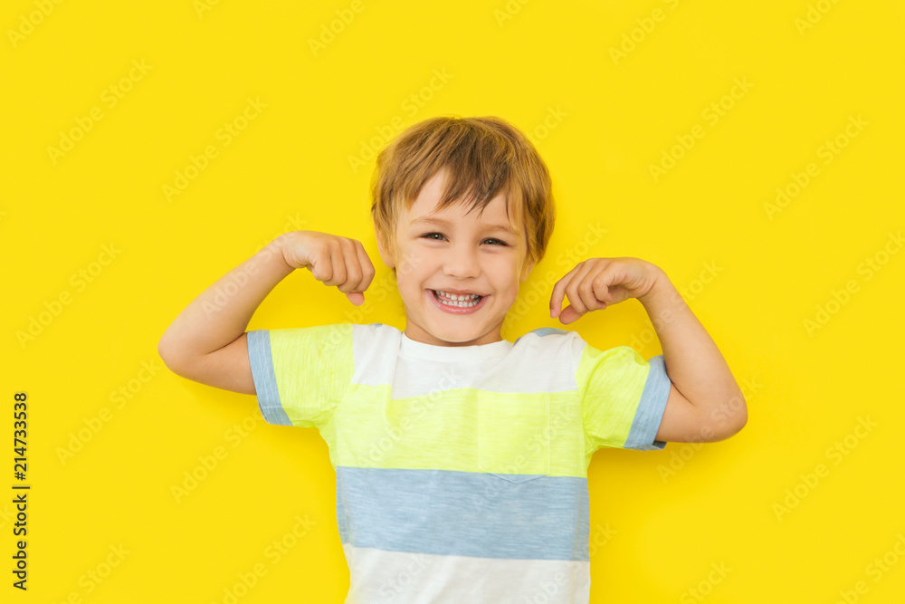 Cute smiling sport child boy showing his biceps on a yellow background ...
