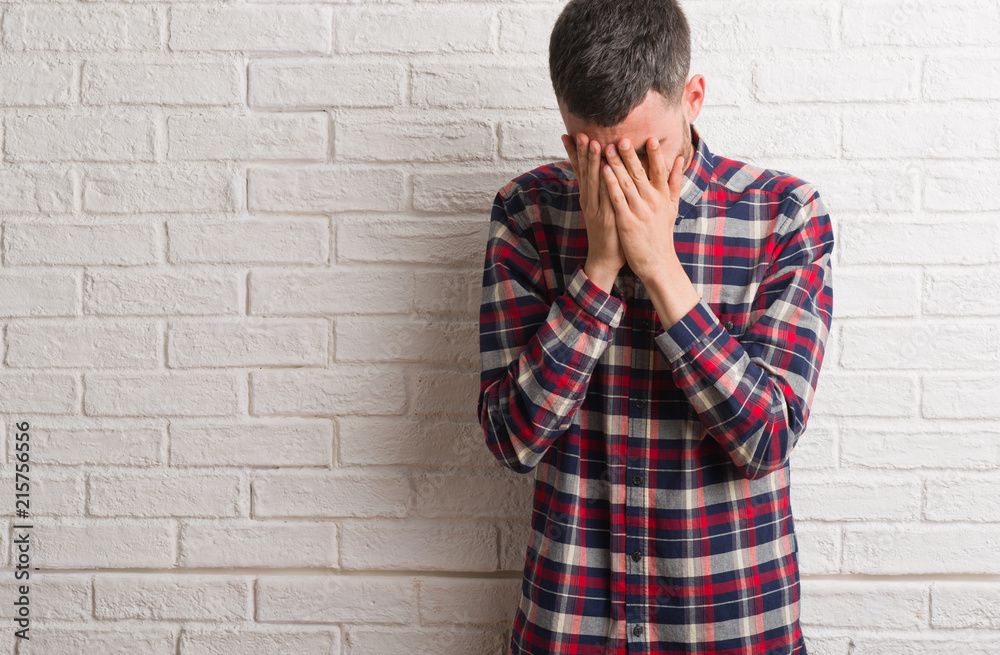 Young adult man standing over white brick wall with sad expression ...